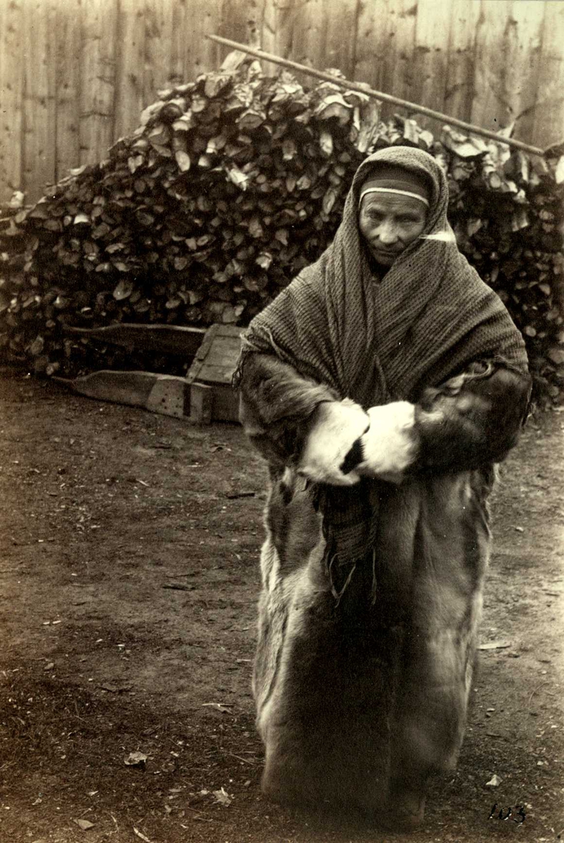 Norge. Kvinne i samisk drakt, står foran vedstabel. - Norsk Folkemuseum ...