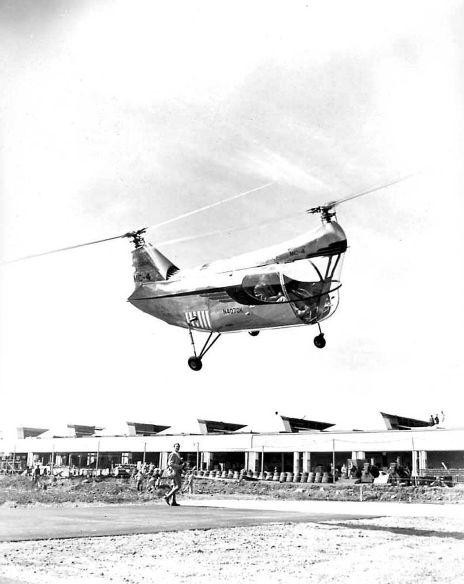 1 helikopter i luften. McCulloch MC-4. 1 person i cockpiten. Bygning ...