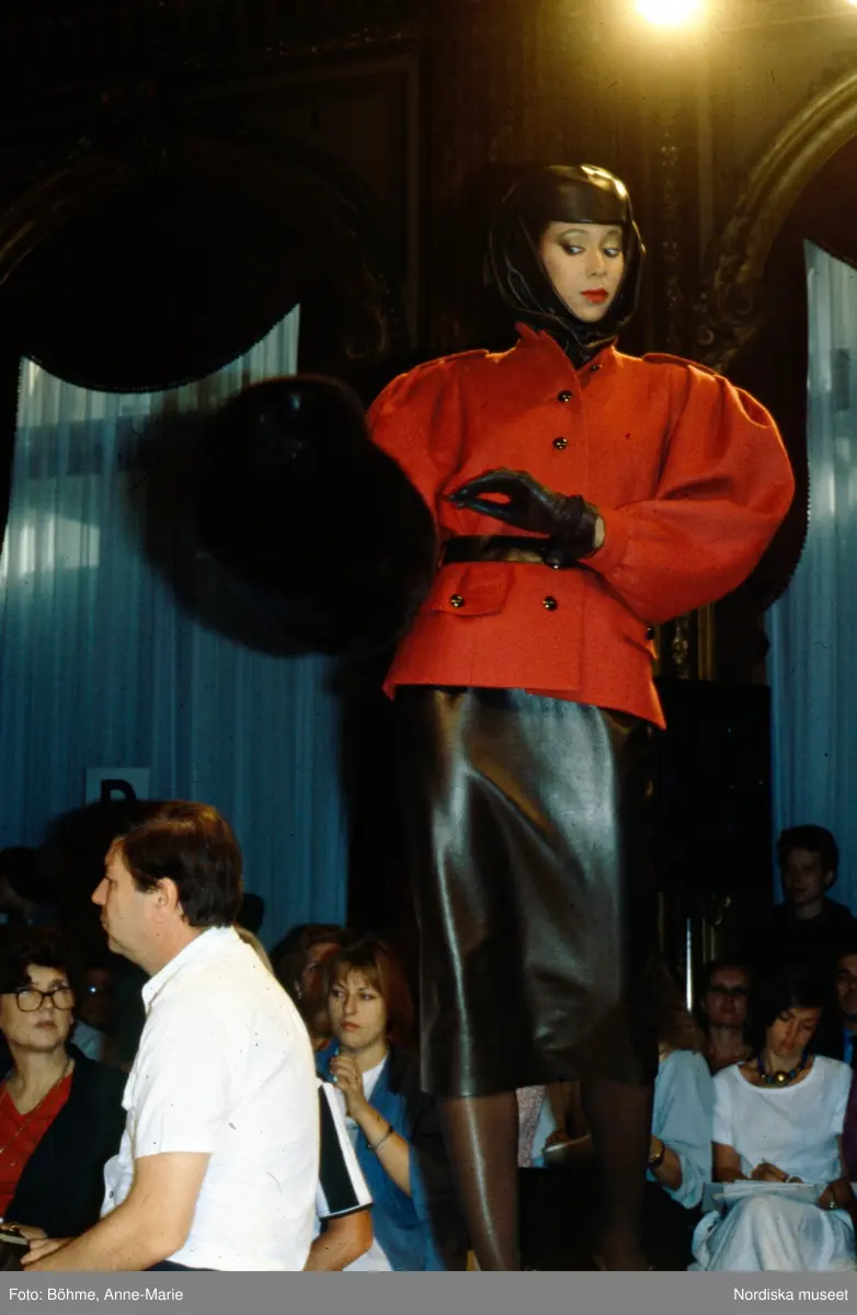 Modevisning. Modell i röd jacka med skärp, svart skinnkjol, handskar ...