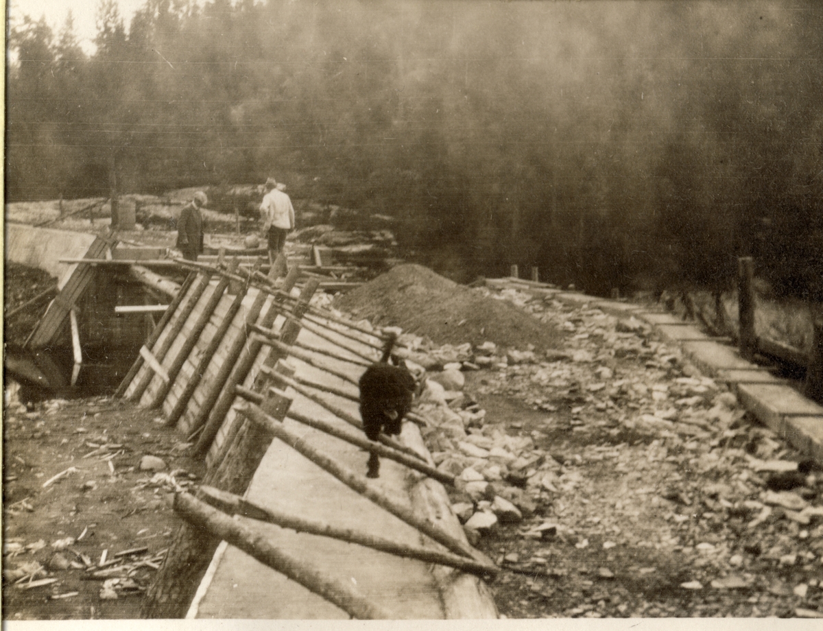 Tre byggearbeidere driver med byggearbeid, antagelig bygging av demning ...