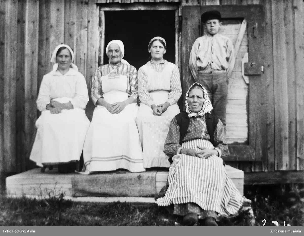 Fyra kvinnor och en pojke, troligen utanför en fäbodstuga i Stöde. Tre ...