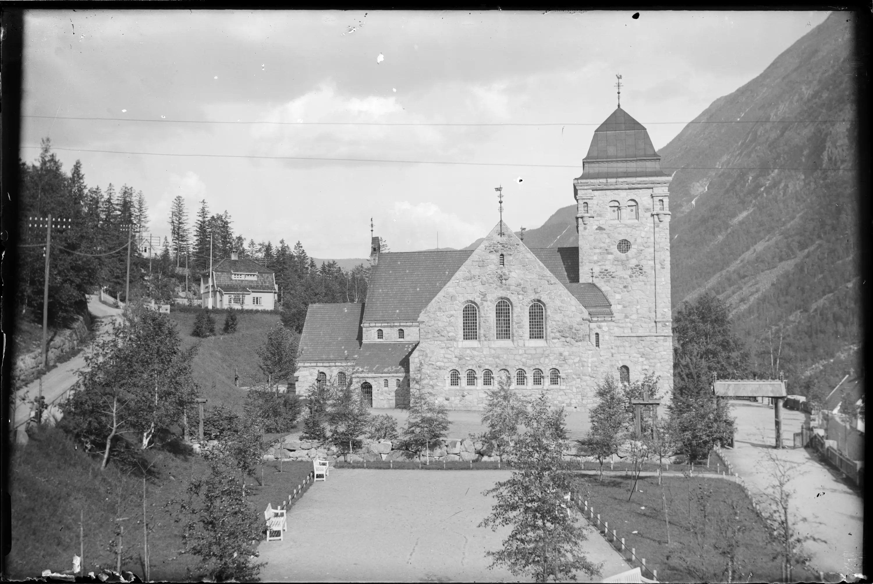 Rjukan kirke med park og grusplass foran kirken. Portal i tre inn på ...