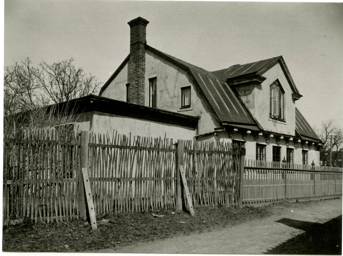 Ett bostadshus med mansardtak år 1908. Runt byggnaden finns ett staket ...