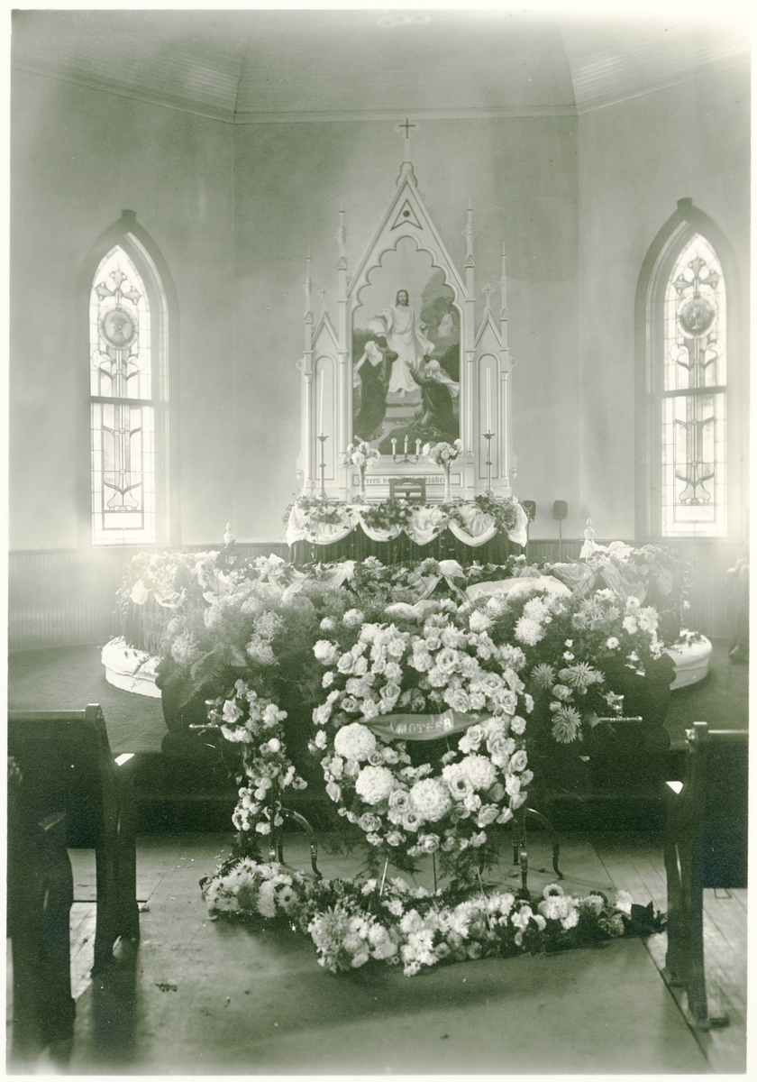 Begravelse. Mye blomster rundt kista. "Mother" står skrevet på et ...