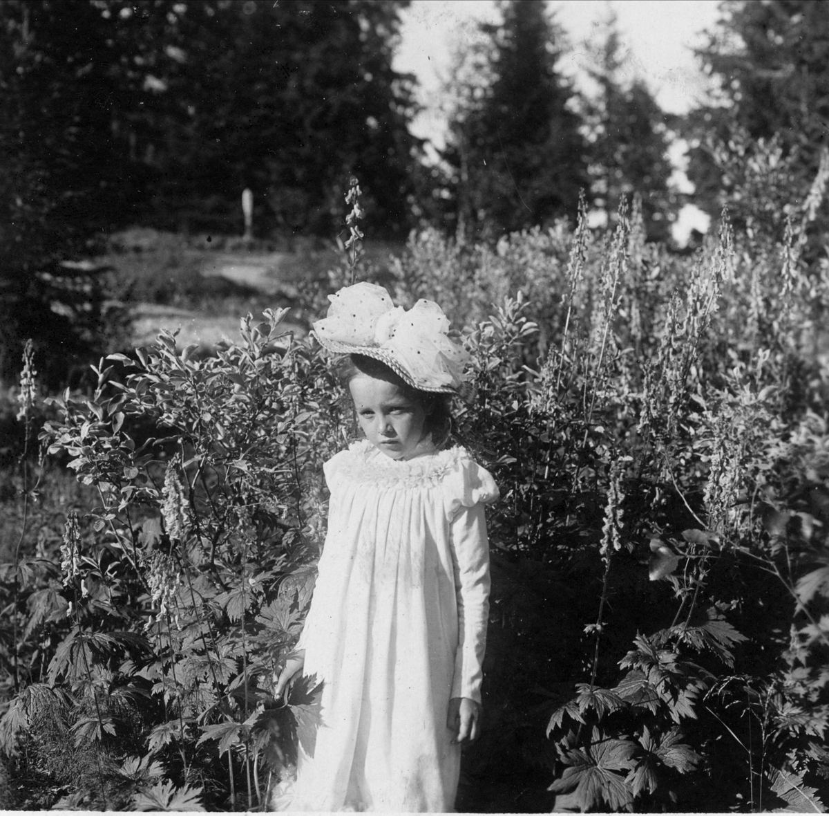 Pike med hatt stående i eng, ukjent sted. Serie tatt av Robert Collett ...