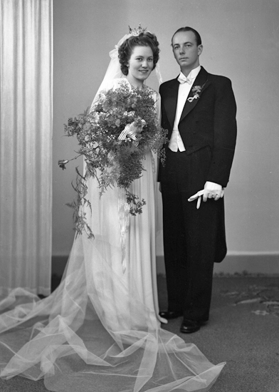 Foto av ett brudpar. Hon är klädd i vit brudklänning, slöja och brudkrona. Han bär frack ...